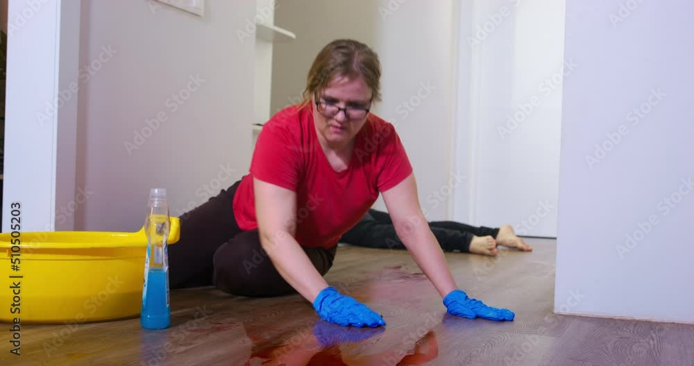 Plump woman washes blood stain from wooden parquet near corpse ...