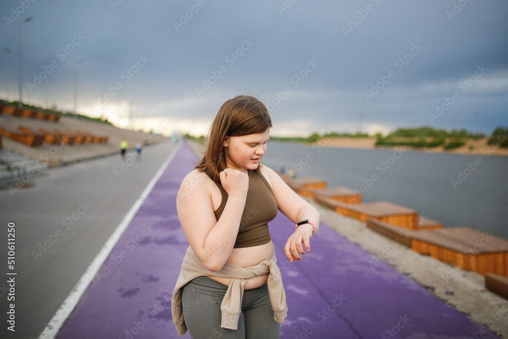 European teenage girl overweight on jog on treadmill along embankment ...