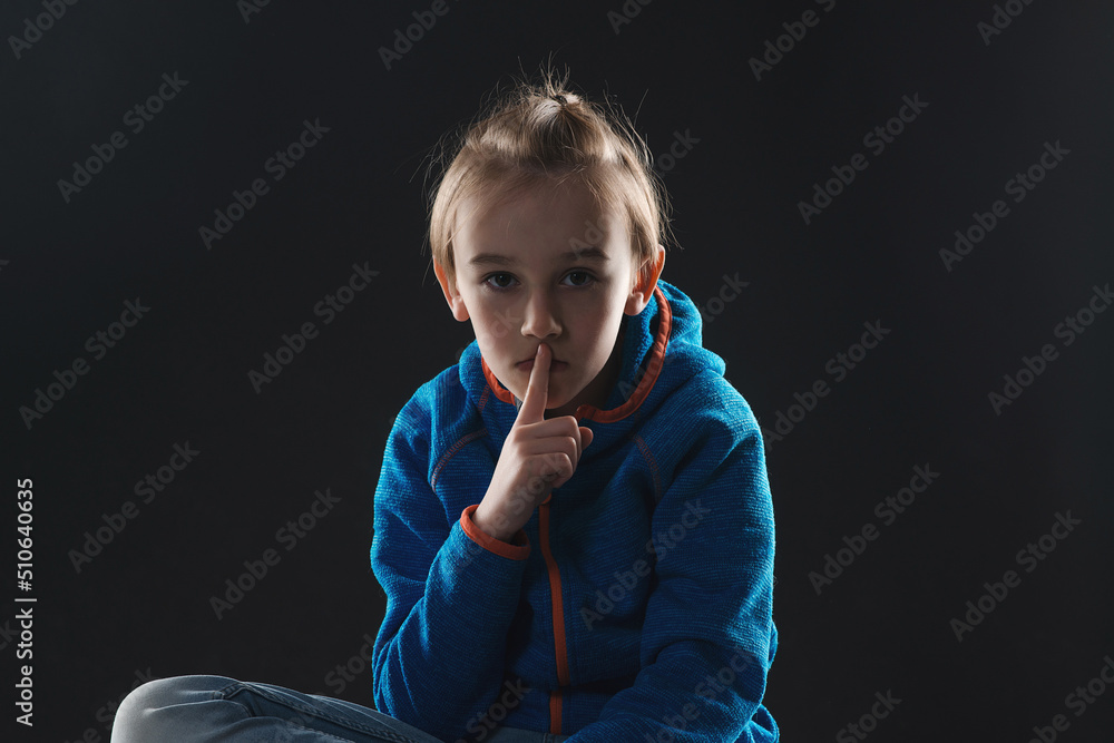 Unhappy young boy with a finger on lips. Sad afraid child sitting quiet ...