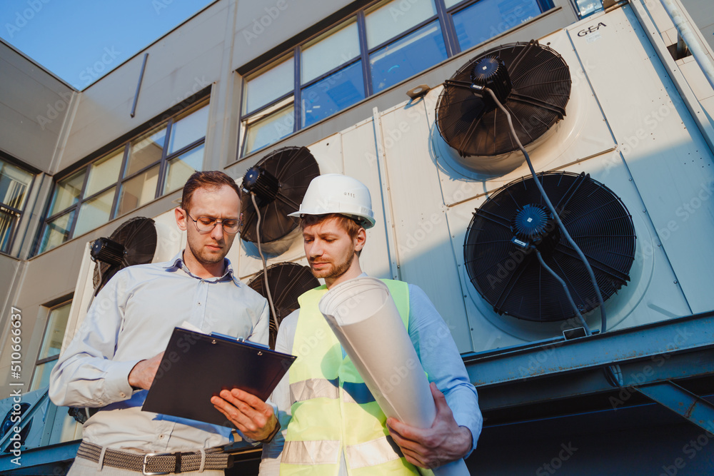 Service engineers in uniform inspecting industrial refrigeration system ...
