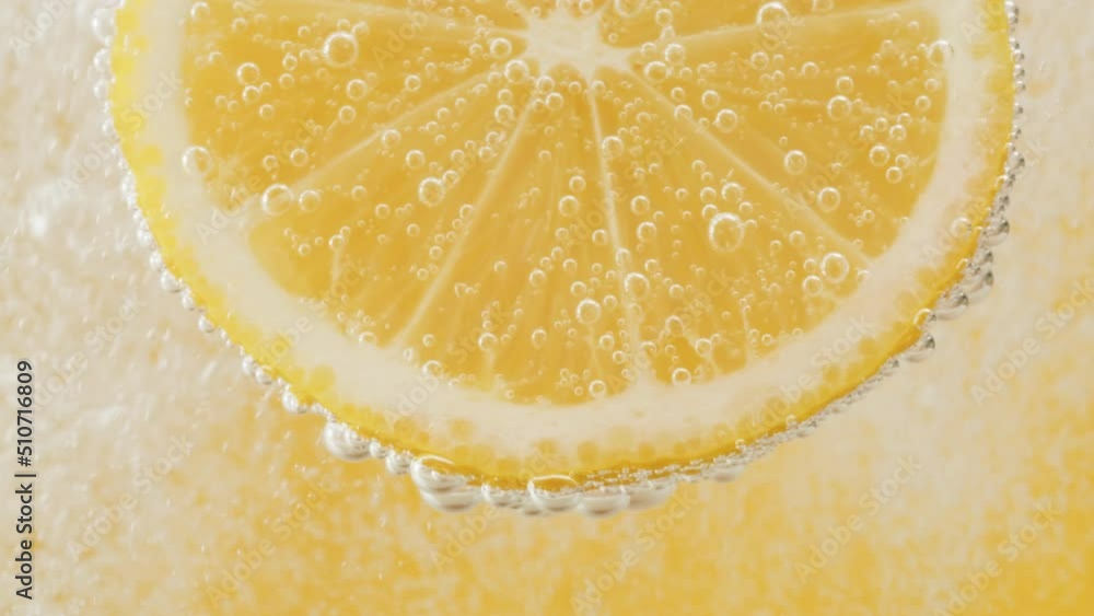 Lemon slice in carbonated water on yellow background, fizzy summer drink, making cocktail of ...