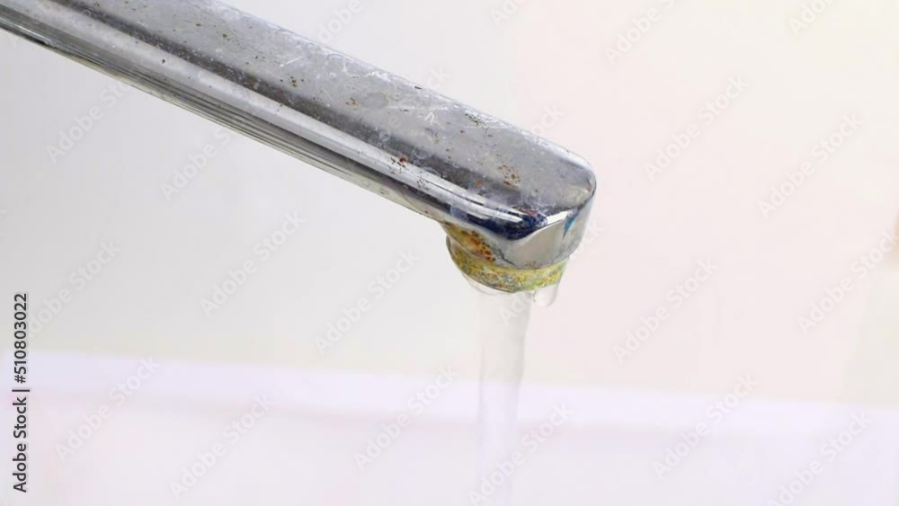 An old rusty water tap is open and a stream of clean water flows into ...