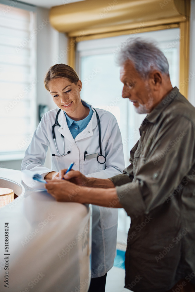 Smiling doctor and her senior patient at reception desk at medical ...