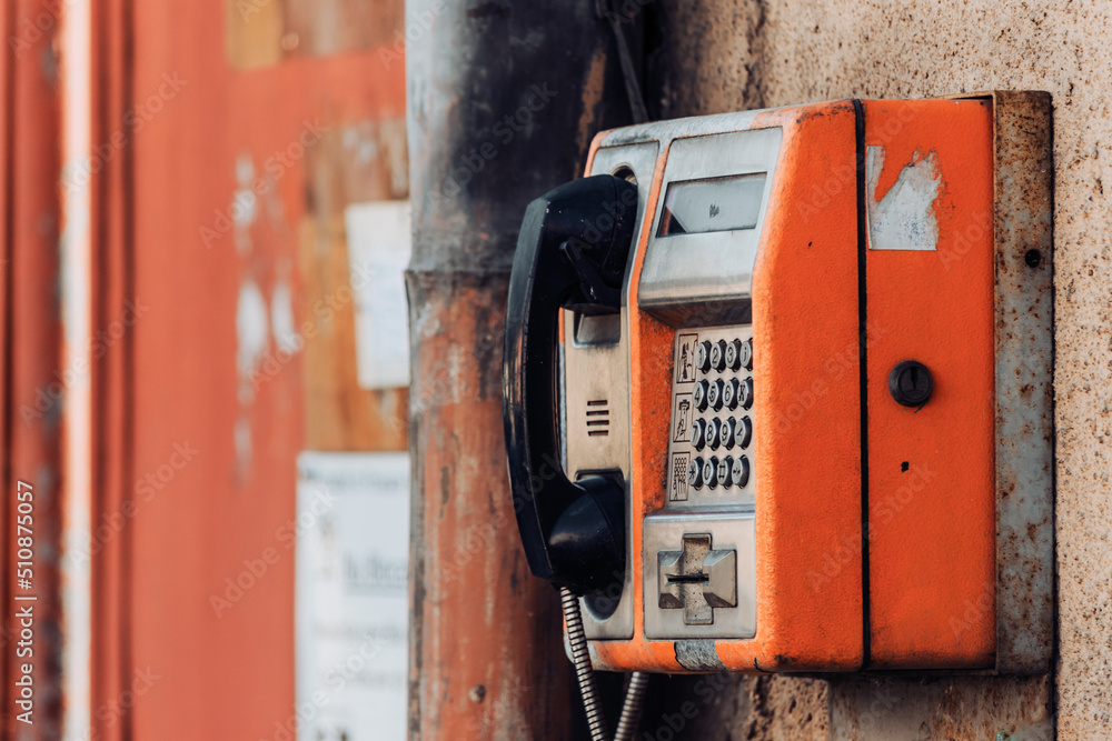 Vintage orange payphone mounted on the exterior wall of a building ...