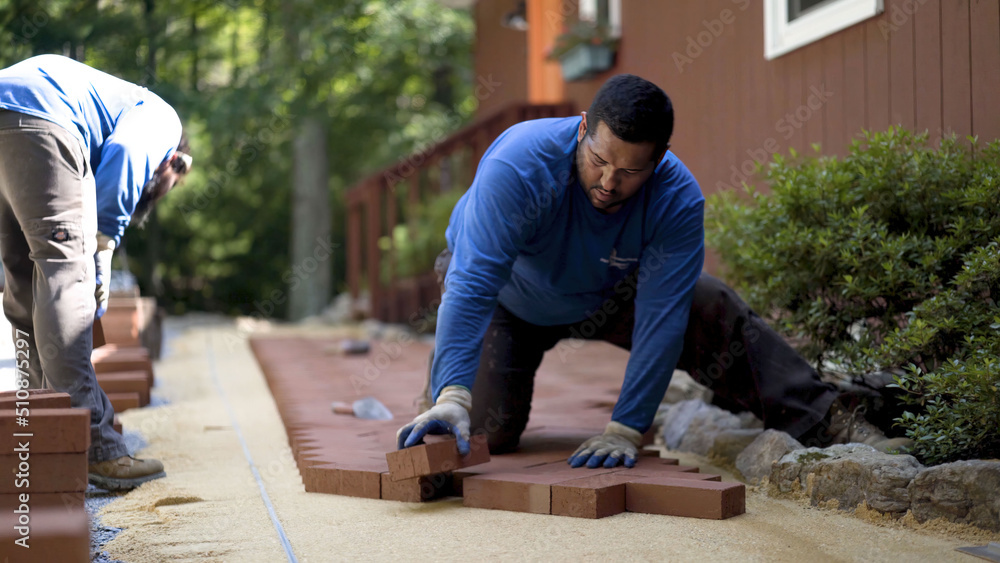 Man putting brick pavers into place in a herringbone pattern in a ...