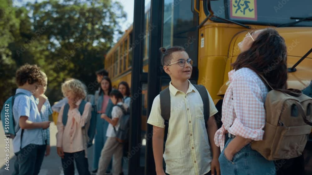 Two pupils stand chatting at schoolbus waiting bus boarding. Friends ...
