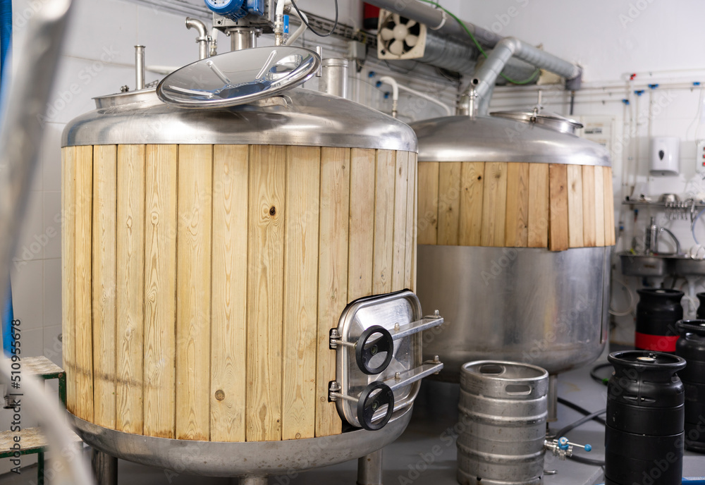 Cylindrical steel fermenters with wood trim and kegs in brewery shop ...
