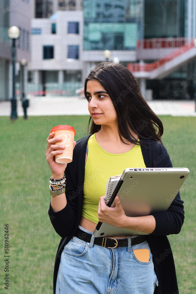 Young girl student walking on campus with laptop computer and cup of ...