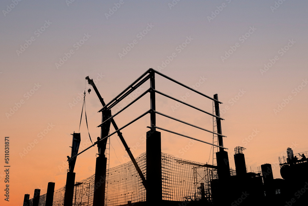 Silhouette of construction workers installing steel roof structure of a ...