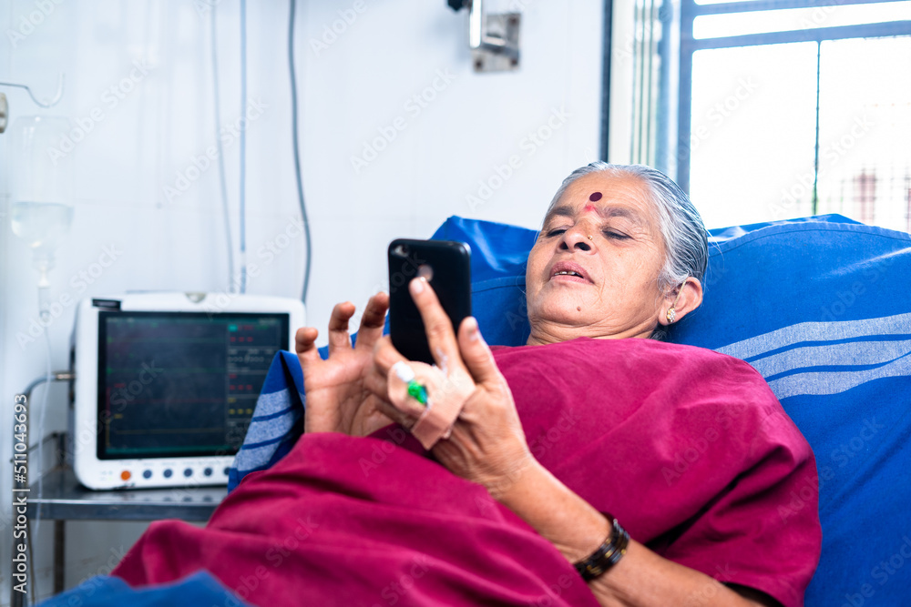 Serious sick woman using mobile phone at hospital while sleeping on bed ...