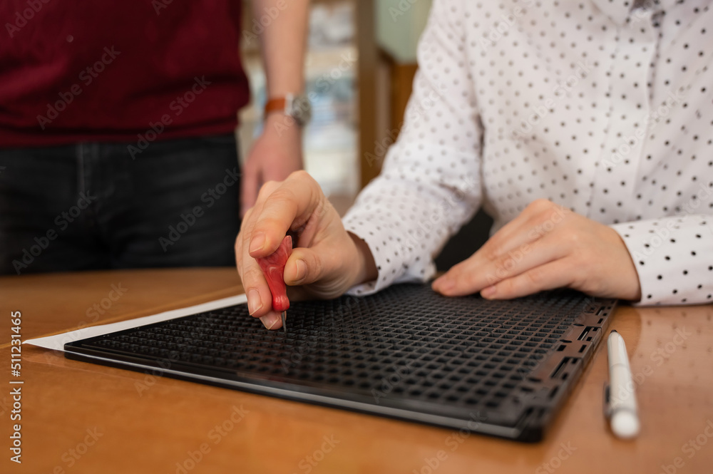 A man teaches a woman how to use a special stencil and stylus to write ...