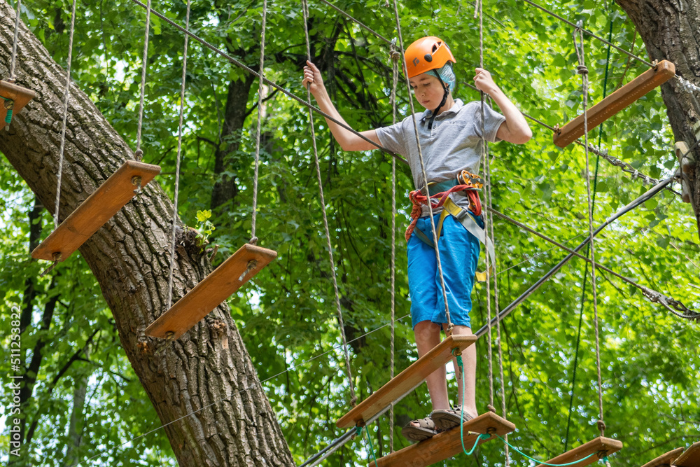 Rope park. A boy teenager in a helmet walks on suspended rope ladders ...