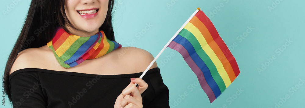 LGBTQ woman holding pride flag standing against a blue green background ...