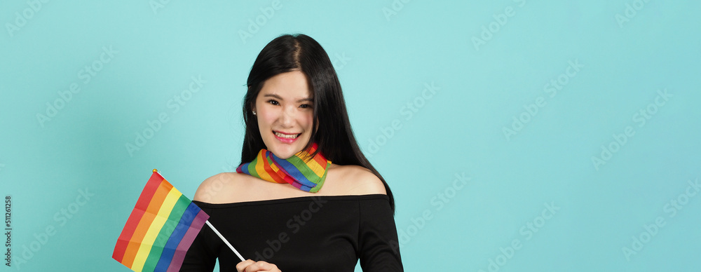 LGBTQ woman holding pride flag standing against a blue green background ...
