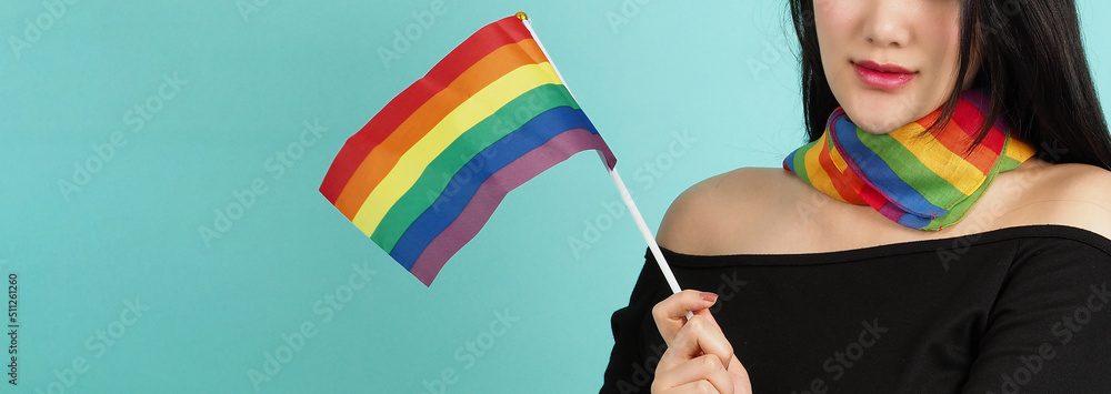 LGBTQ woman holding pride flag standing against a blue green background ...