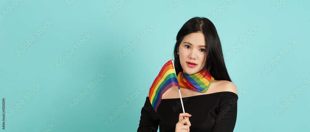 LGBTQ woman holding pride flag standing against a blue green background ...