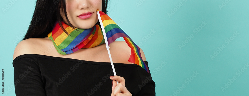 LGBTQ woman holding pride flag standing against a blue green background ...