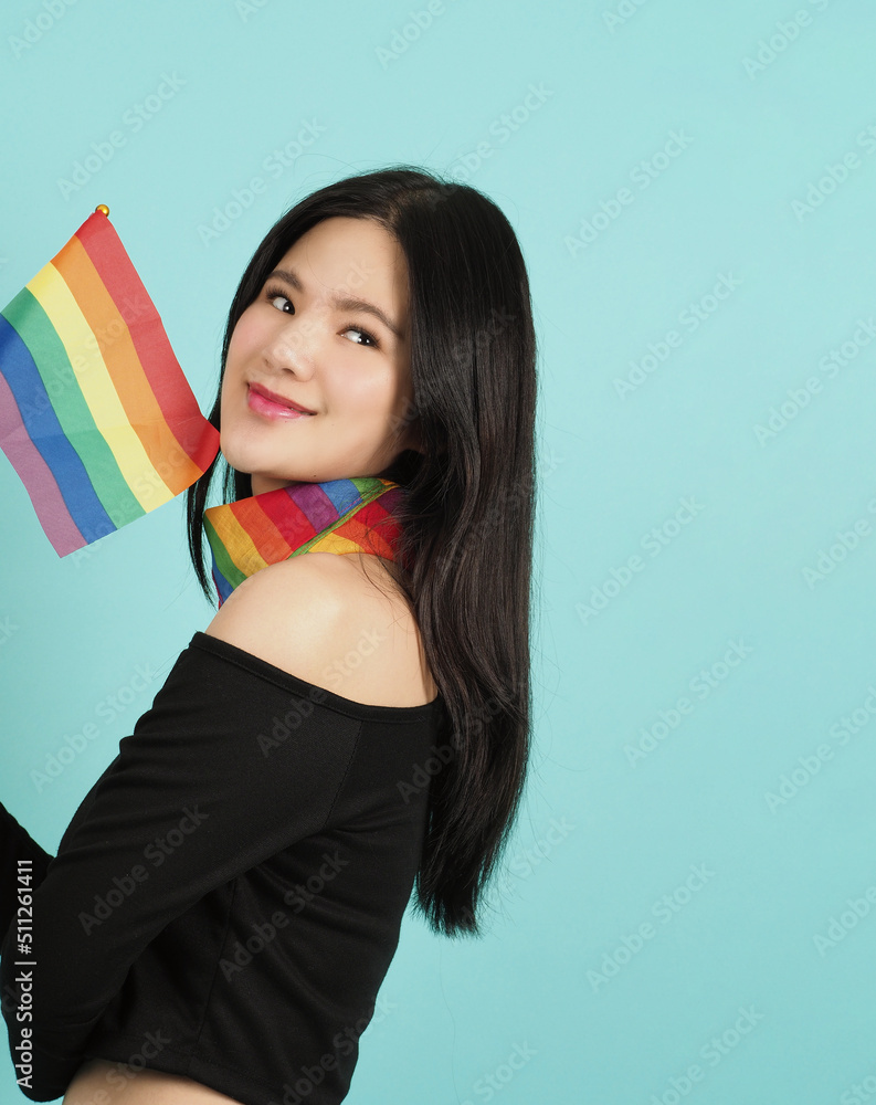 LGBTQ woman holding pride flag standing against a blue green background ...