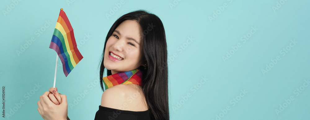 LGBTQ woman holding pride flag standing against a blue green background ...