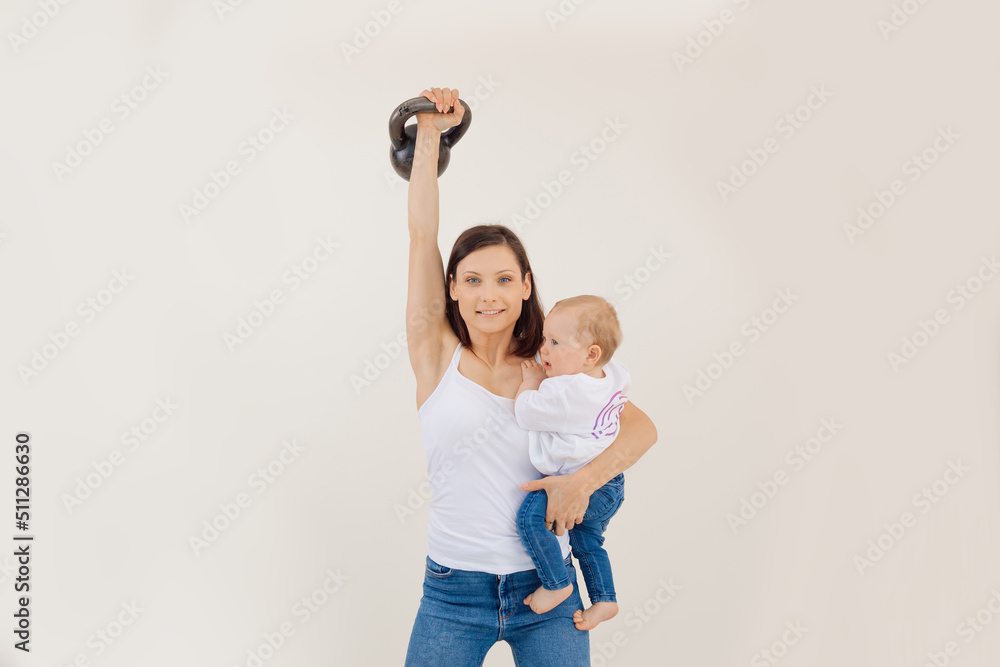Young athletic smiling woman lifting up kettlebell and holding little ...