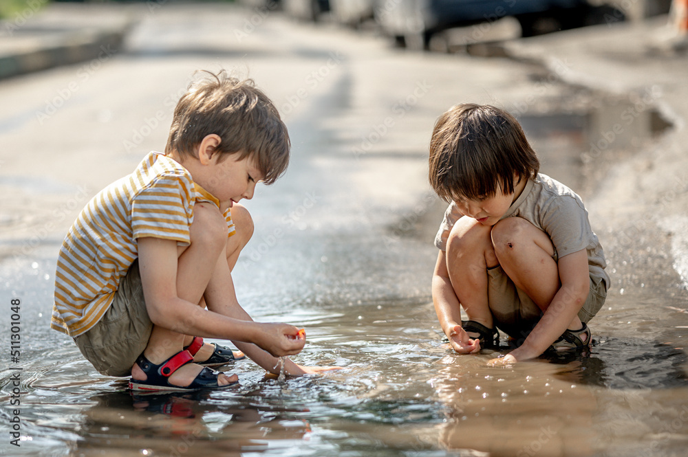 two boys, two brothers playing in a puddle. Happy children are walking ...