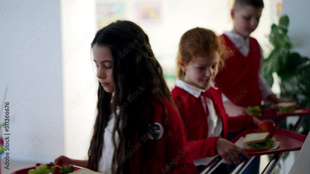 Happy schoolchildren standing in queue with trays and receiving lunch ...