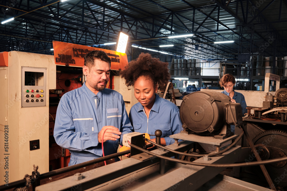 Asian male and female African American engineers in safety uniform work by inspecting machines ...