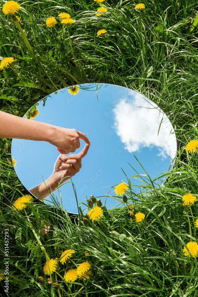 nature concept - hand touching sky reflection in round mirror on summer ...