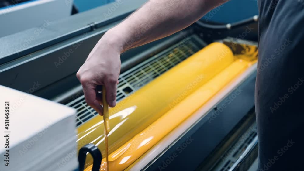 A worker in a printing house applies yellow ink to a packaging printing ...