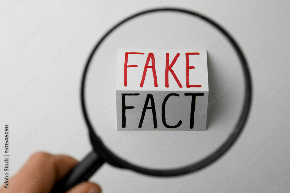 Woman holding magnifying glass over sheet of paper with words Fact and ...