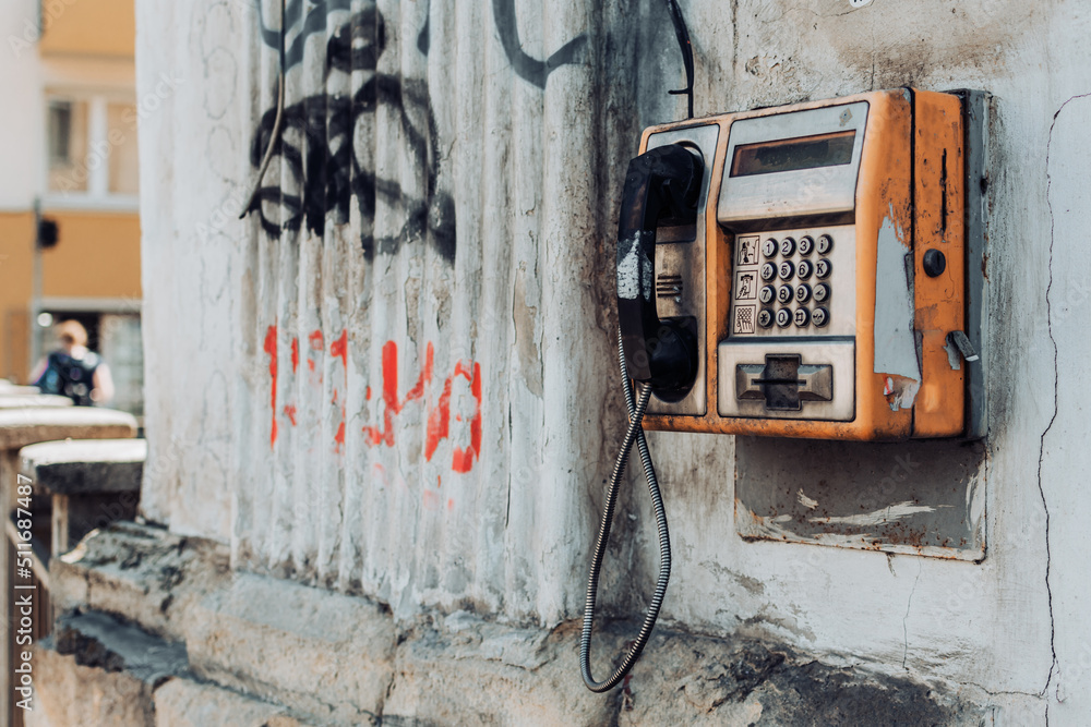 Old orange payphone in a rough neighborhood installed on the exterior ...