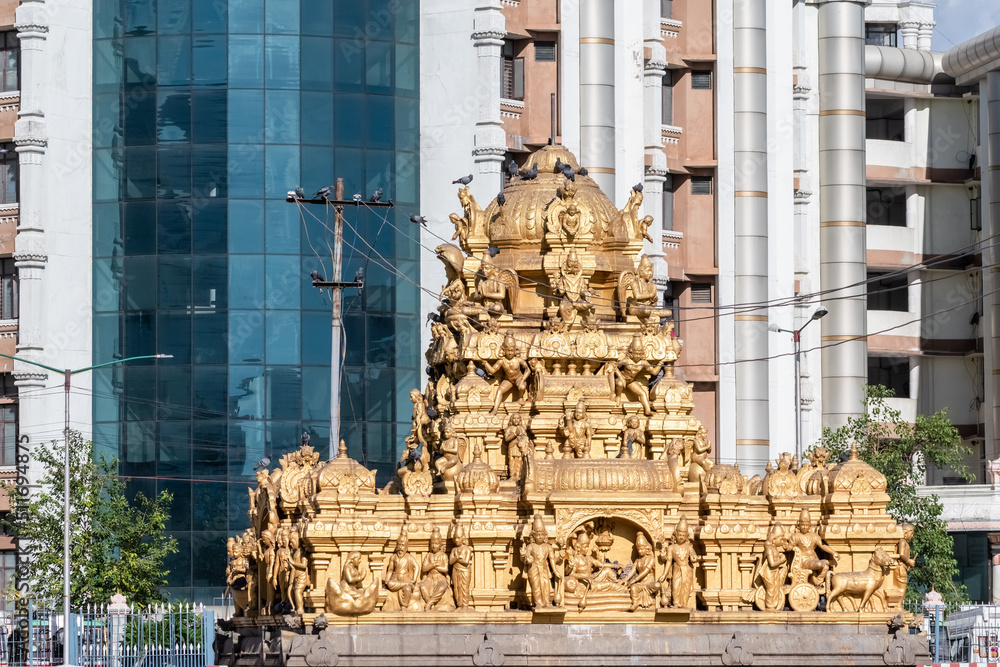 The golden spire of a Hindu temple with a modern building in the ...