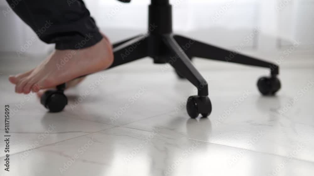Barefoot men's feet on an office chair with wheels on white porcelain ...
