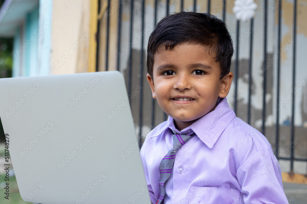 portrait of Indian school kid in uniform having laptop doing online ...