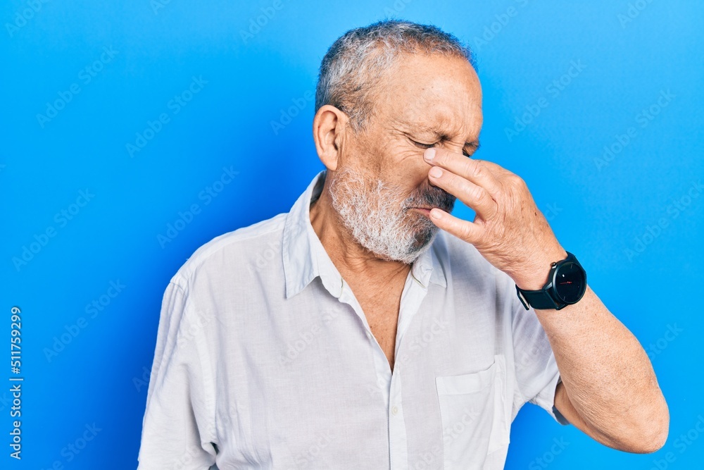 Handsome senior man with beard wearing casual white shirt smelling ...