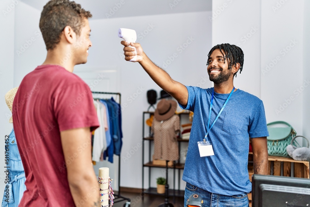 Two men shopkeeper and customer measuring temperature at clothing store ...