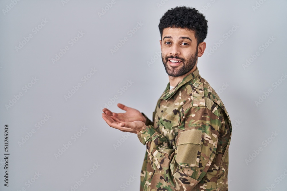 Arab man wearing camouflage army uniform pointing aside with hands open ...
