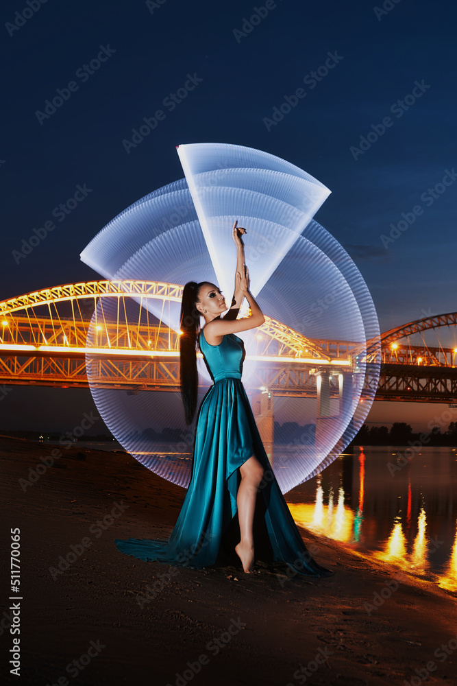 Girl in an evening dress poses against the backdrop of a bridge. Photo ...