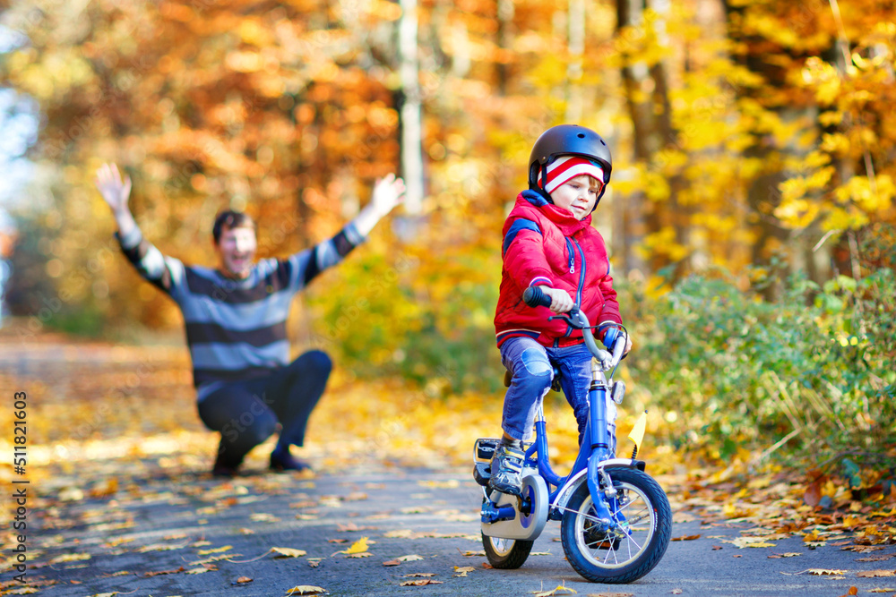 Little kid boy learning moving on bicycle. His father teaching his son ...