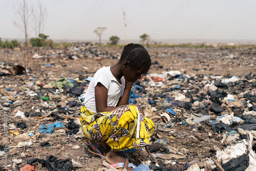 Exhausted little African girl kneeling in a garbage dump where she is ...