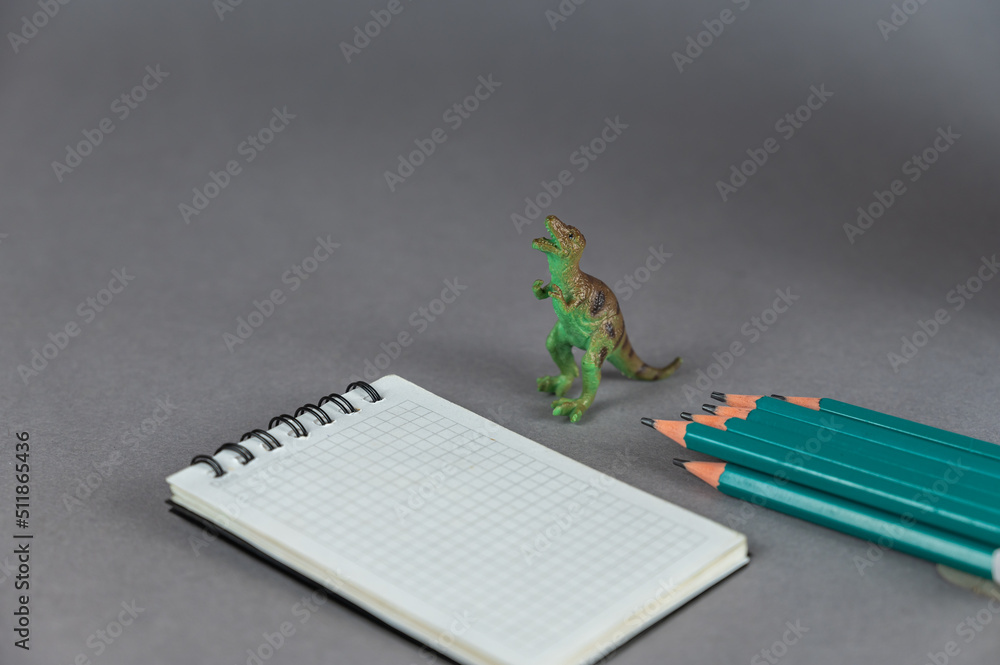 A miniature dinosaur, a set of pencils and a notebook against a gray ...
