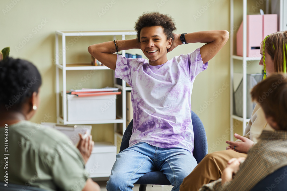 African teenage boy sitting on chair and smiling, he behaving badly ...