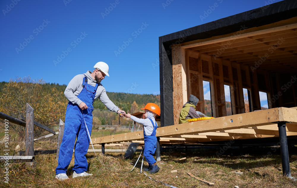 Father with toddler son building wooden frame house on pile foundation ...