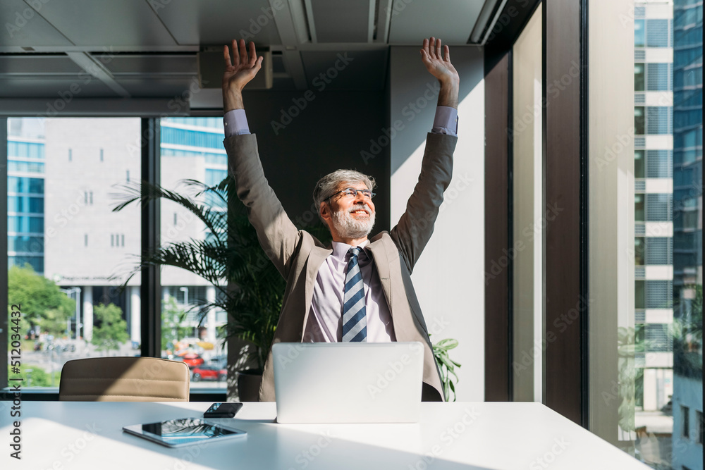 Happy businessman sitting with arms raised at desk in office Stock ...