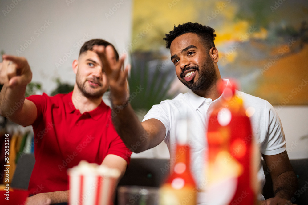 Smiling roommates talking with each other watching football match at ...