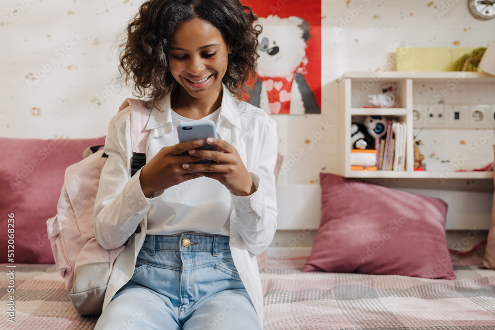 African smiling teen girl sitting on a bed with phone Stock Photo ...