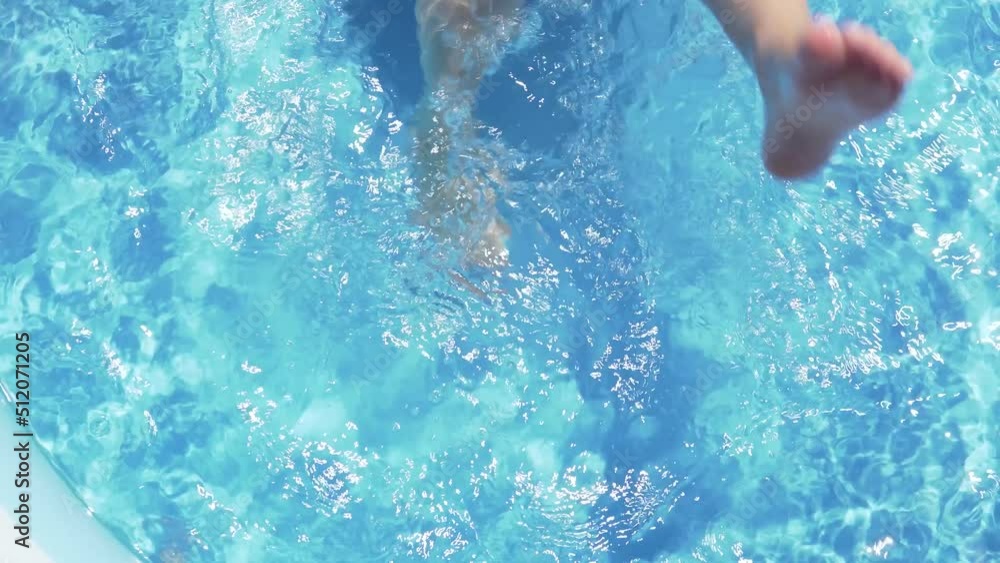 child playing with his feet in the pool kid swimming in the pool summer ...