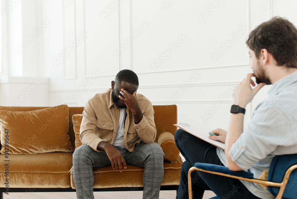 Frustrated young african american man sitting on sofa and holding hands ...