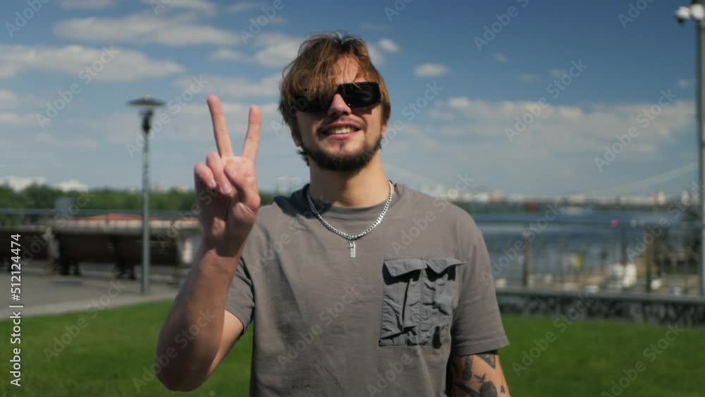 Cheerful smiling caucasian dude with tattoed arm showing the peace sign ...