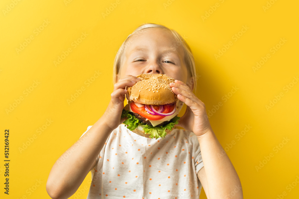 Cute little caucasian girl with blonde hair enjoying burger on a yellow ...